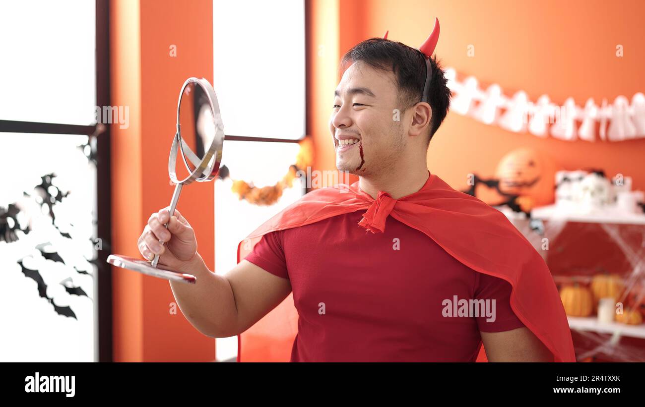 Young chinese man wearing devil costume looking on mirror at home Stock ...