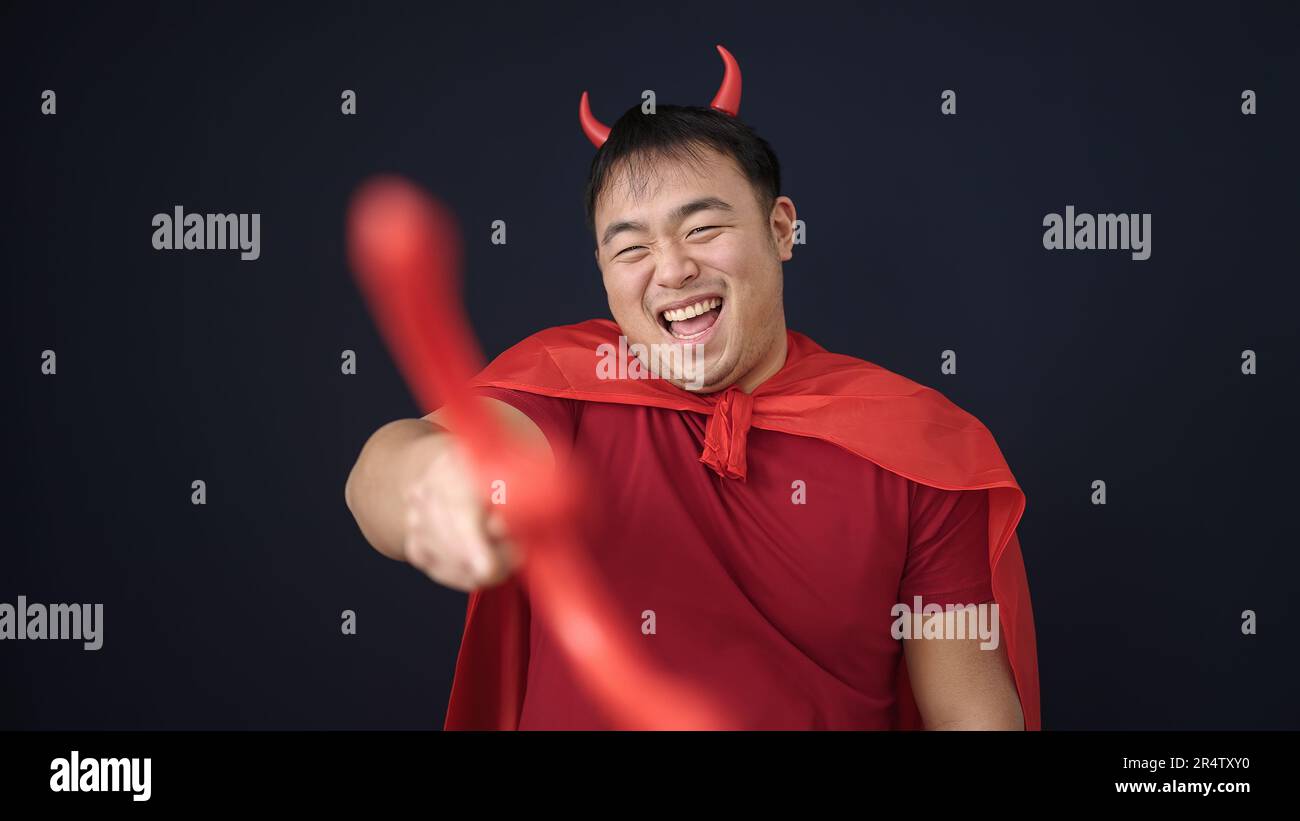 Young chinese man wearing devil costume holding trident over isolated ...