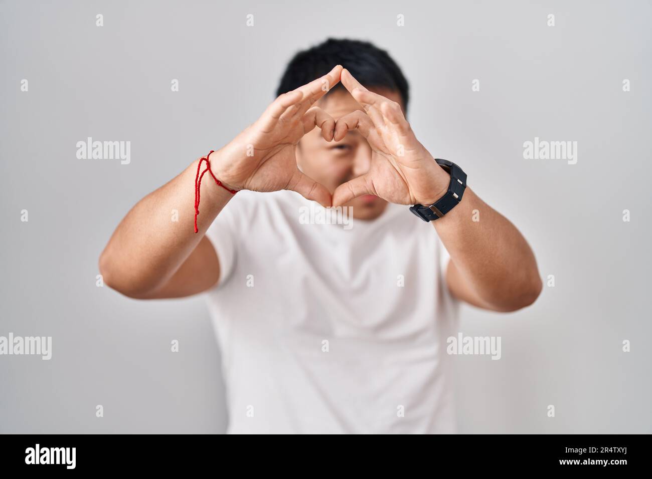 Young chinese man standing over white background doing heart shape with ...