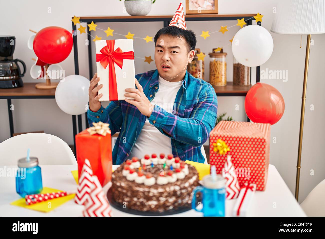 Young chinese man celebrating birthday with cake and present in shock ...