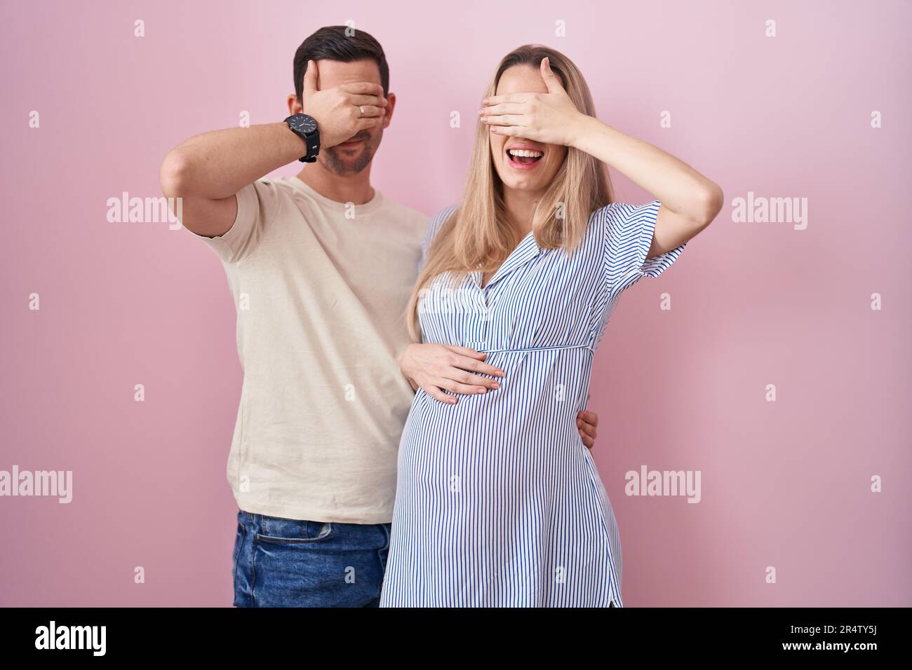 Young couple expecting a baby standing over pink background smiling and ...