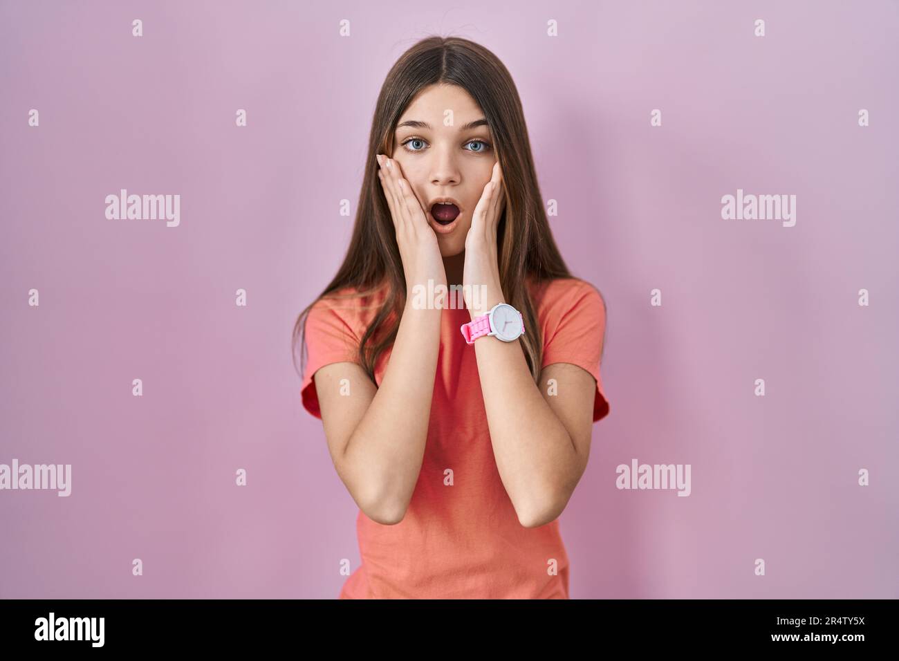 Teenager girl standing over pink background afraid and shocked ...