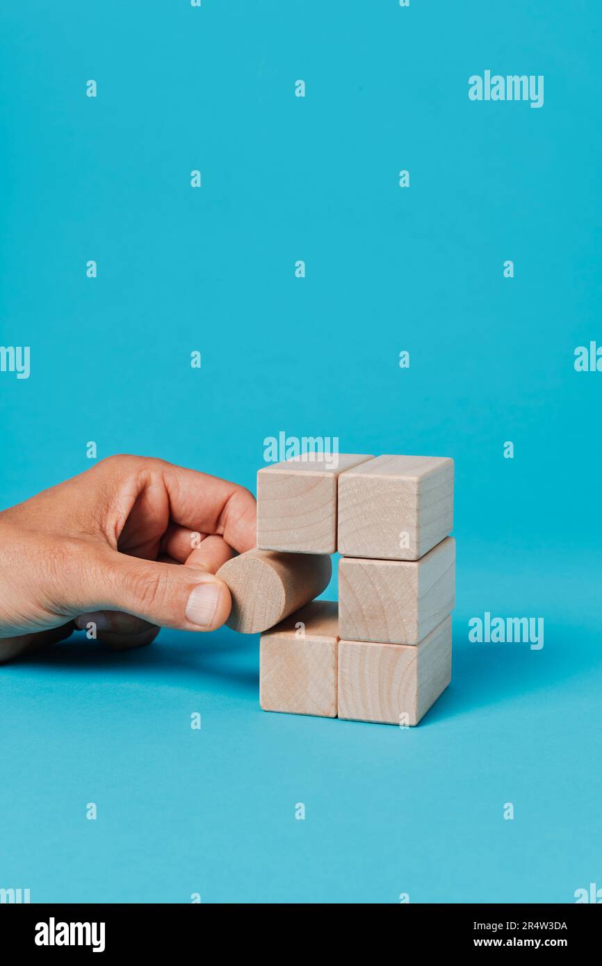 a man puts a cylindrical toy block in a stack of rectangular toy blocks ...