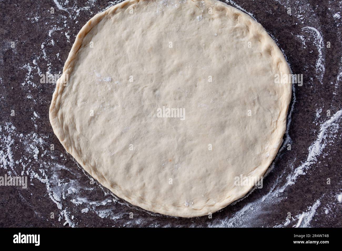 Rolled out pizza dough on floured slate surface, photographed overhead ...