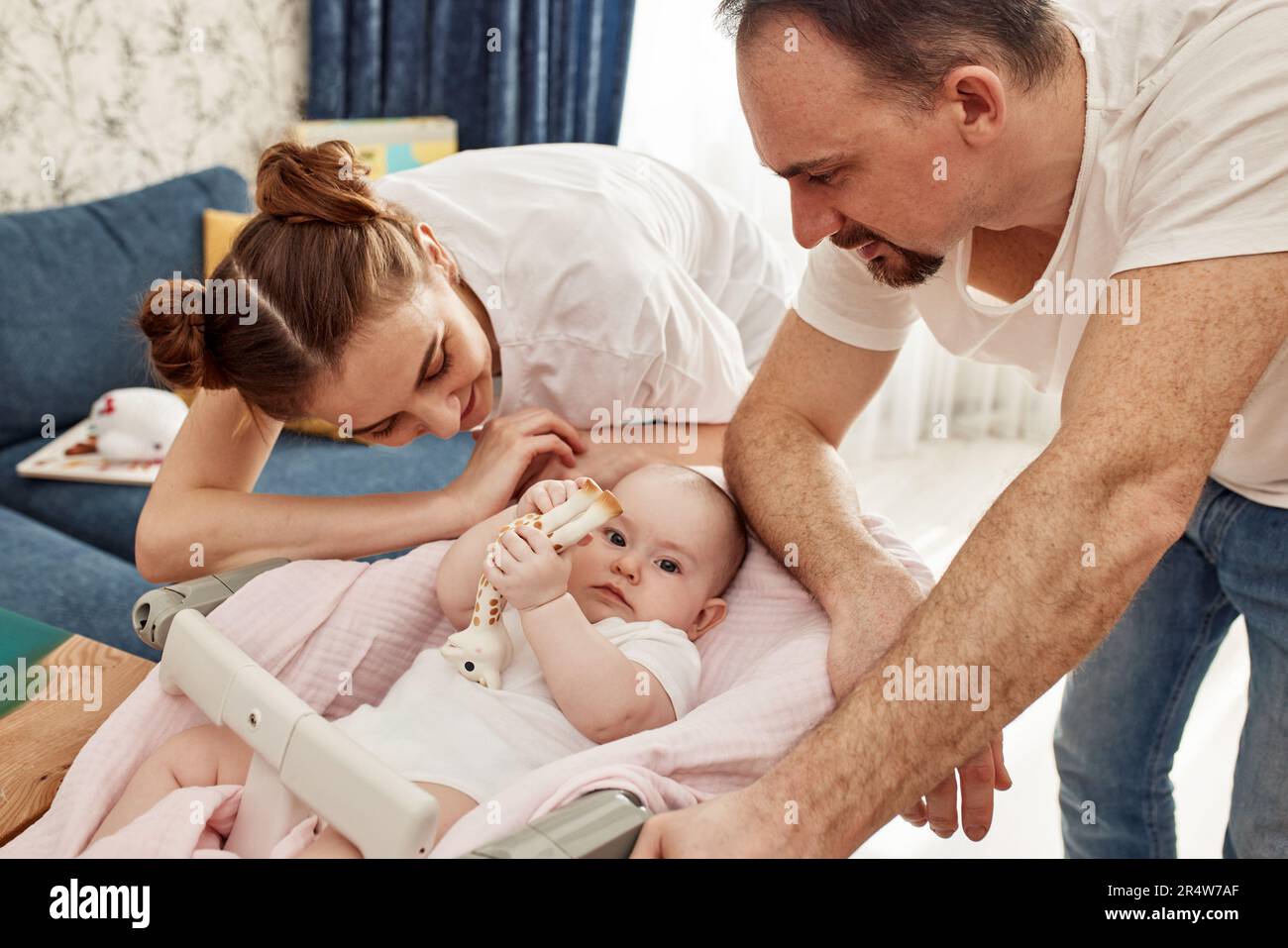 Happy smiling mom and dad leaned over their baby lying in the cradle ...