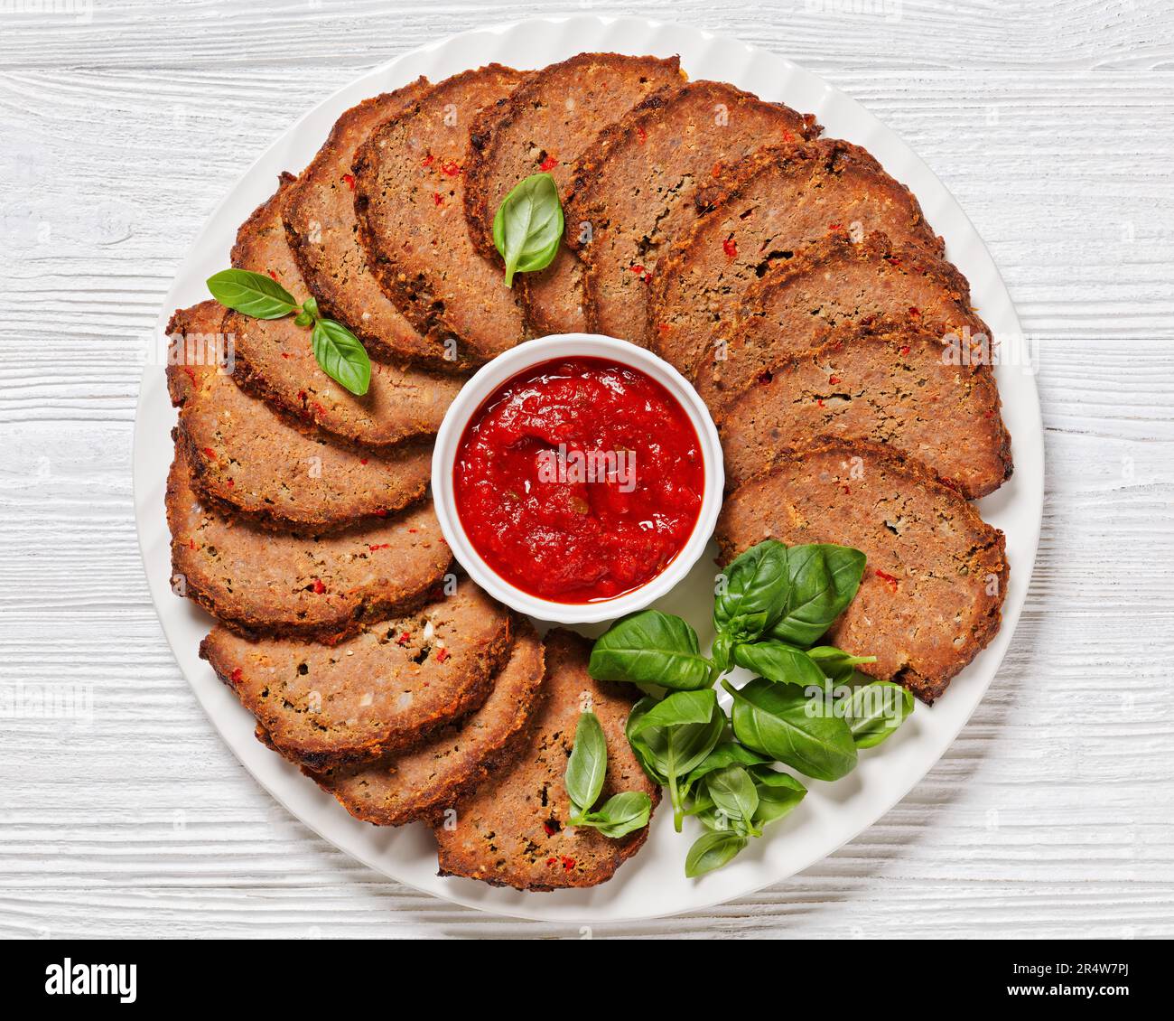 italian style meatloaf cut in slices on white plate on white textured ...