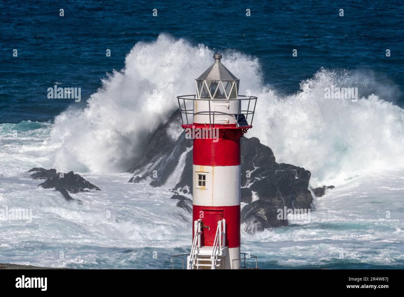 A tall circular lighthouse tower has horizontal red and white colors ...