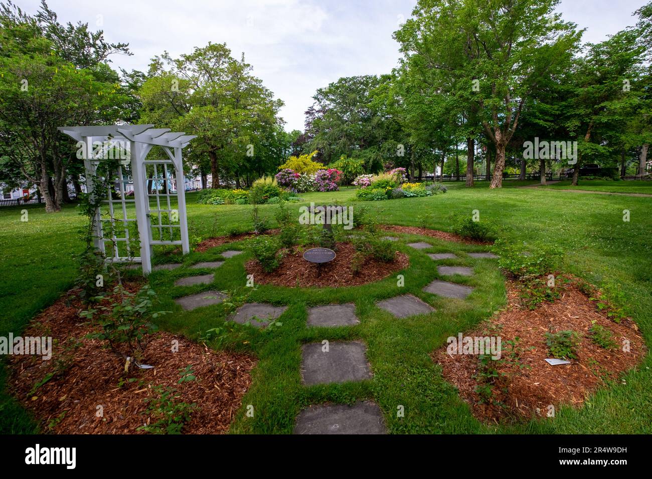 A white wooden archway and square stones form a circle in a garden with ...