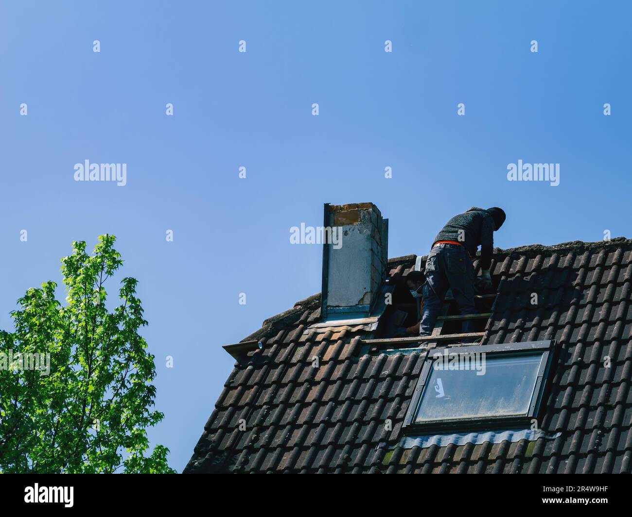 A roofer stands atop a tall house, demolishing the chimney as clear ...
