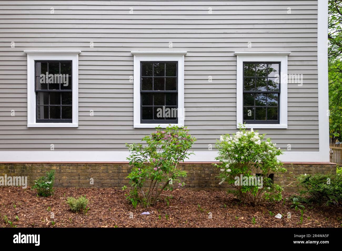 On a tan wooden wall, three double hung windows with black wood frames ...