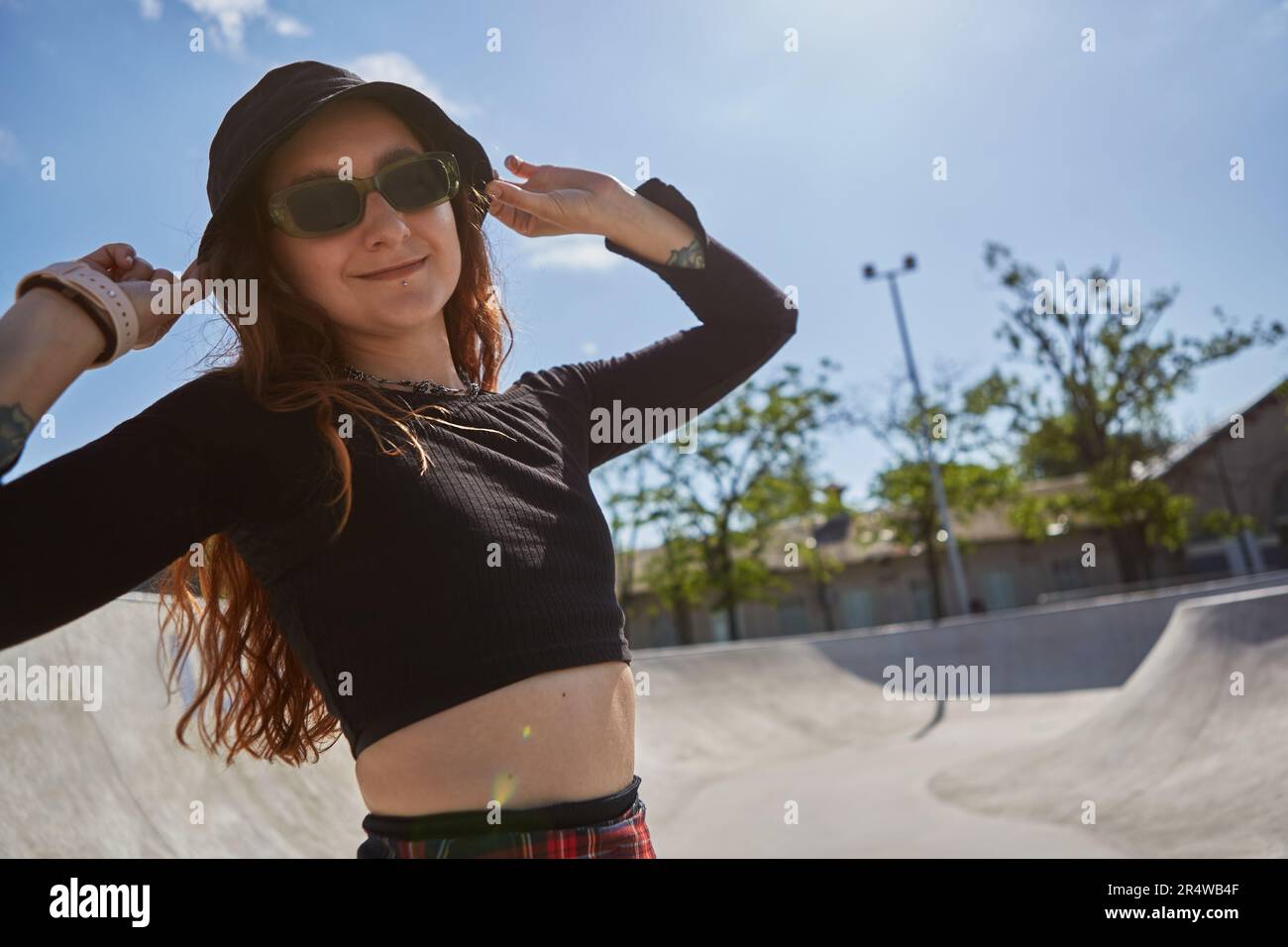Friendly female skater posing in a concrete skatepark in summer ...