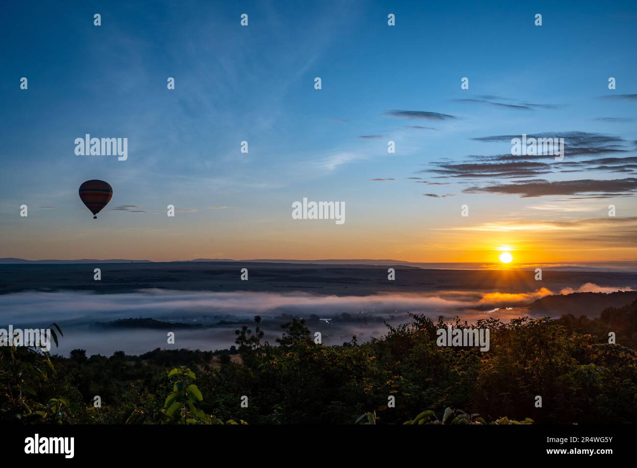 Hot air balloon rising above cloud covered wildness at sunrise. Maasai ...