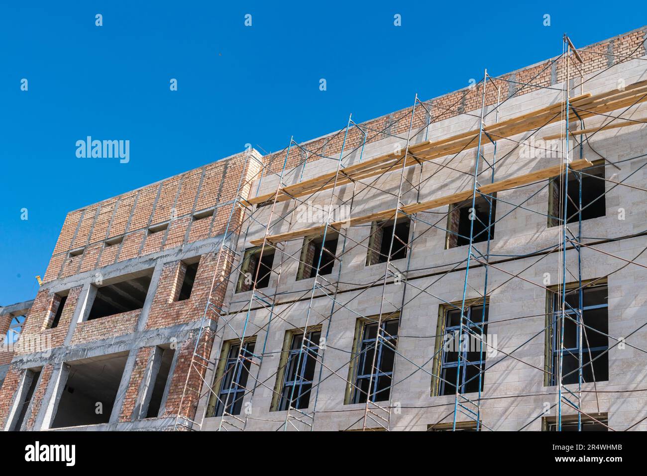 Unfinished brick building under a blue sky framed by scaffolding Stock ...
