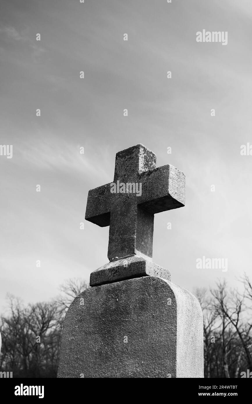 Simple plain stone cross standing in the sunny cemetery in a black and ...