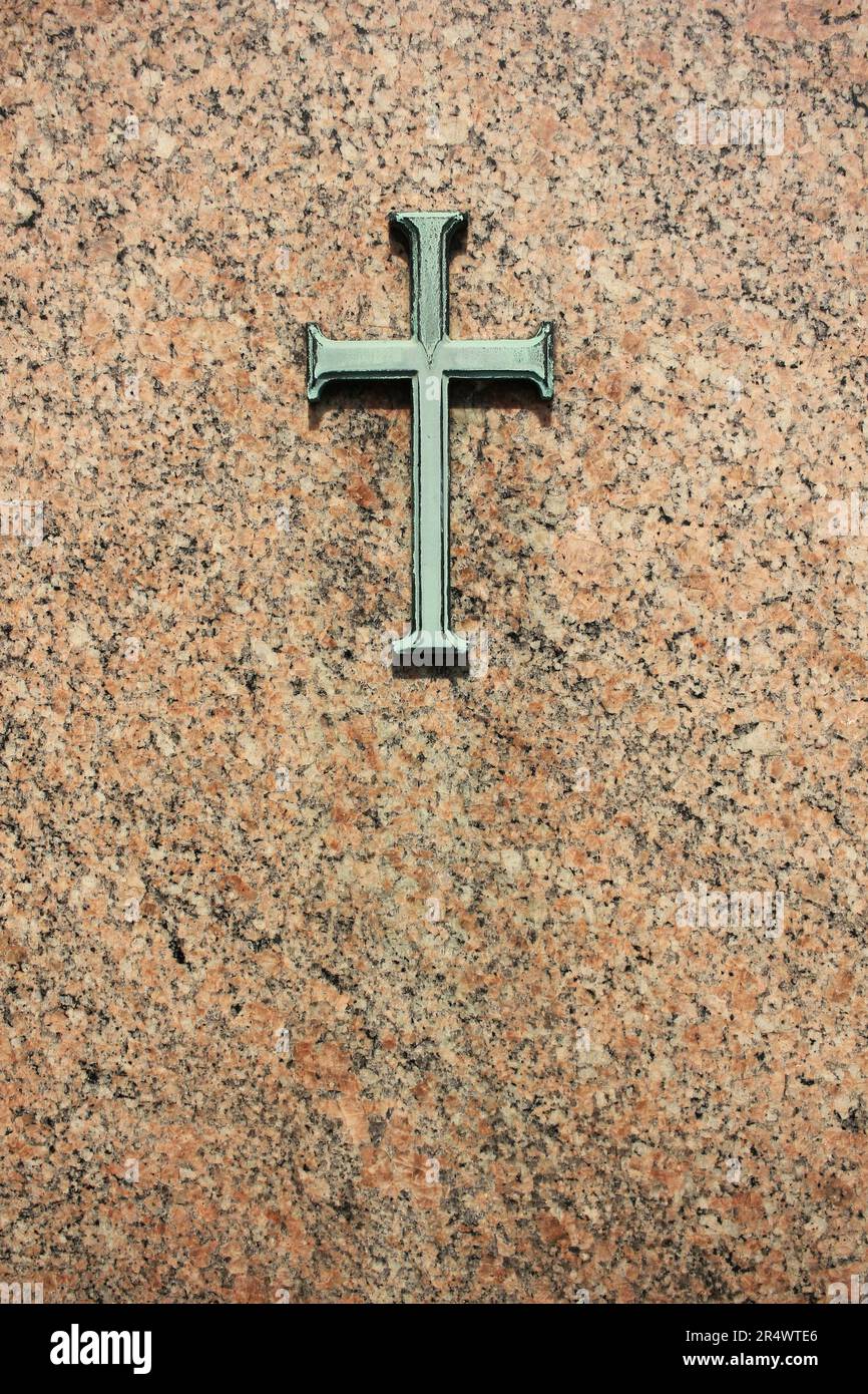 A copper metal Christian cross hanging on a traditional natural granite ...