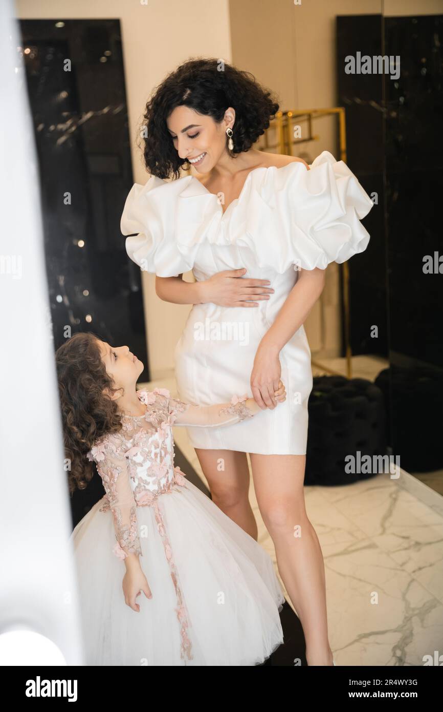 happy and cute middle eastern little girl in floral attire looking at ...