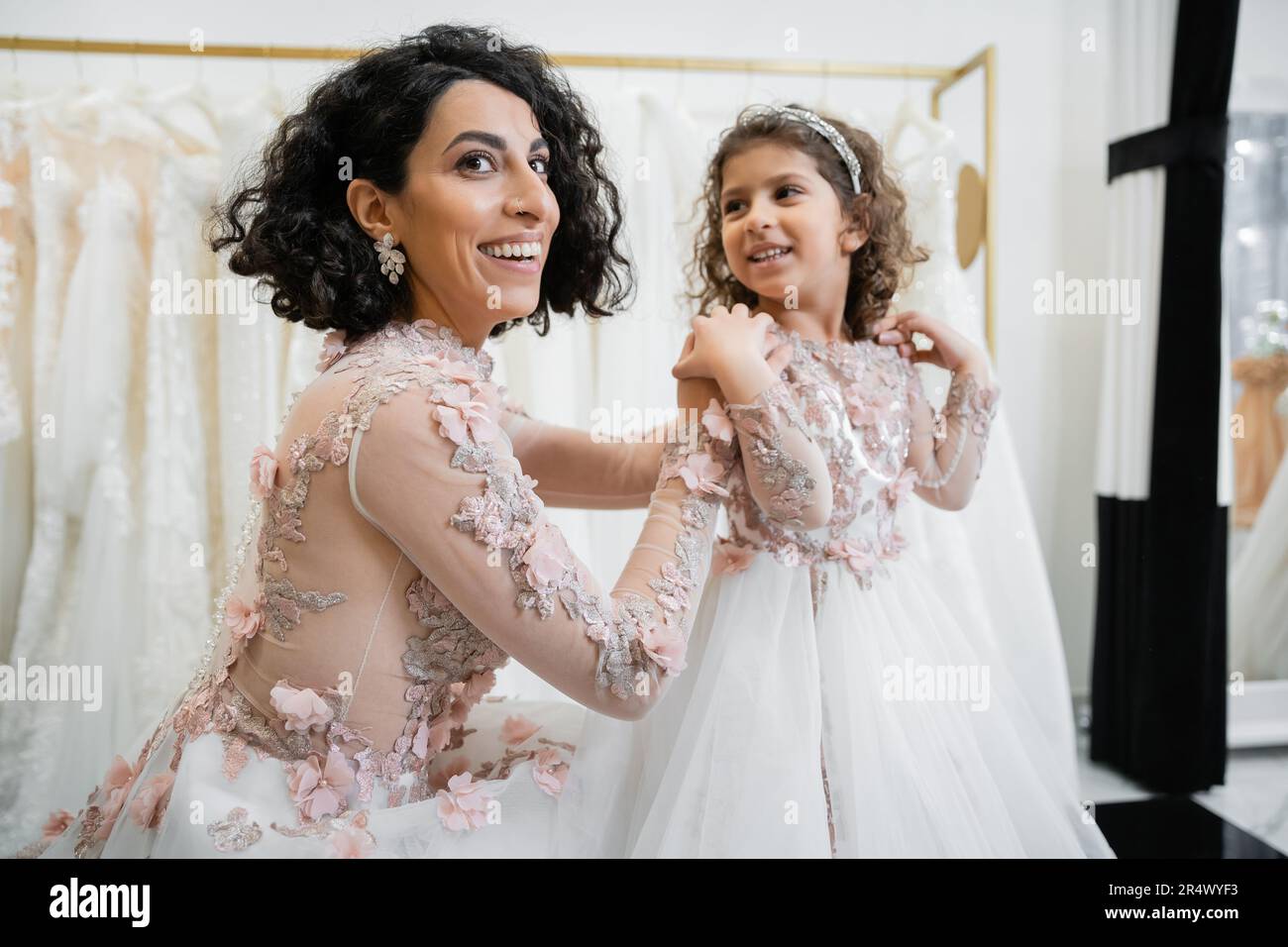 happy middle eastern woman with brunette hair in floral wedding dress ...