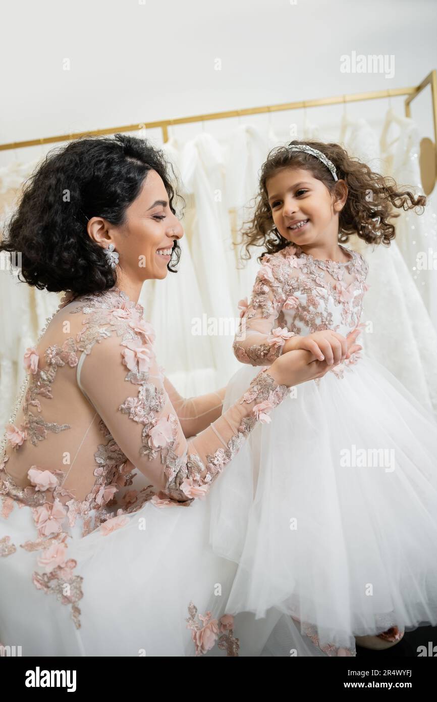 happy middle eastern bride with brunette wavy hair in floral wedding ...