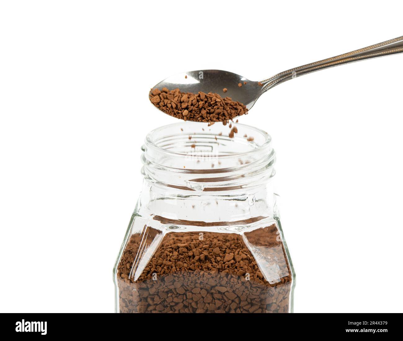 Granulated instant coffee is poured from a spoon into a glass jar of ...