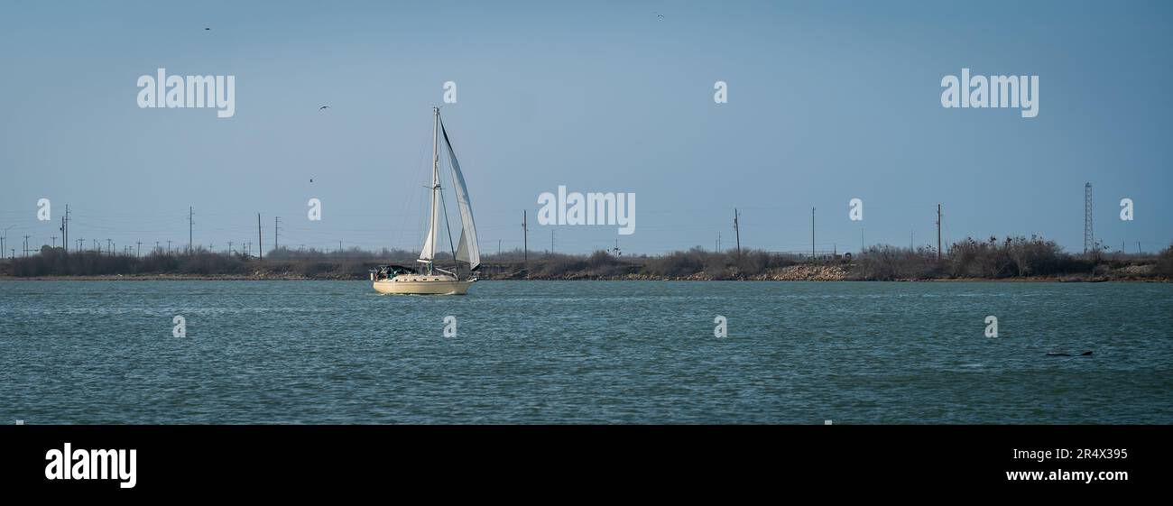 A White Sailboat sailing left to right on the blue water of the ...