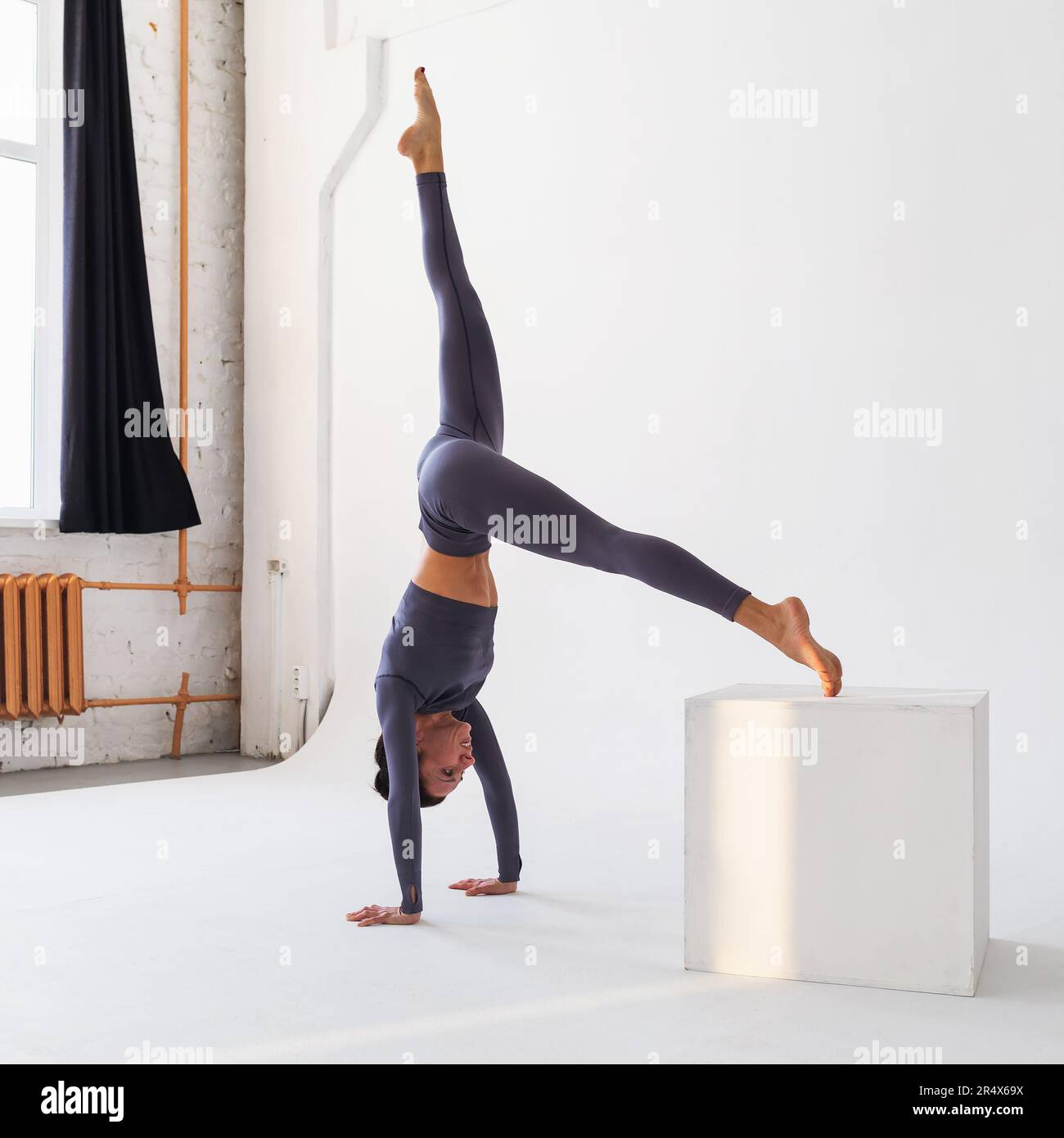 A woman in sportswear performs a handstand and leans with one foot on a ...