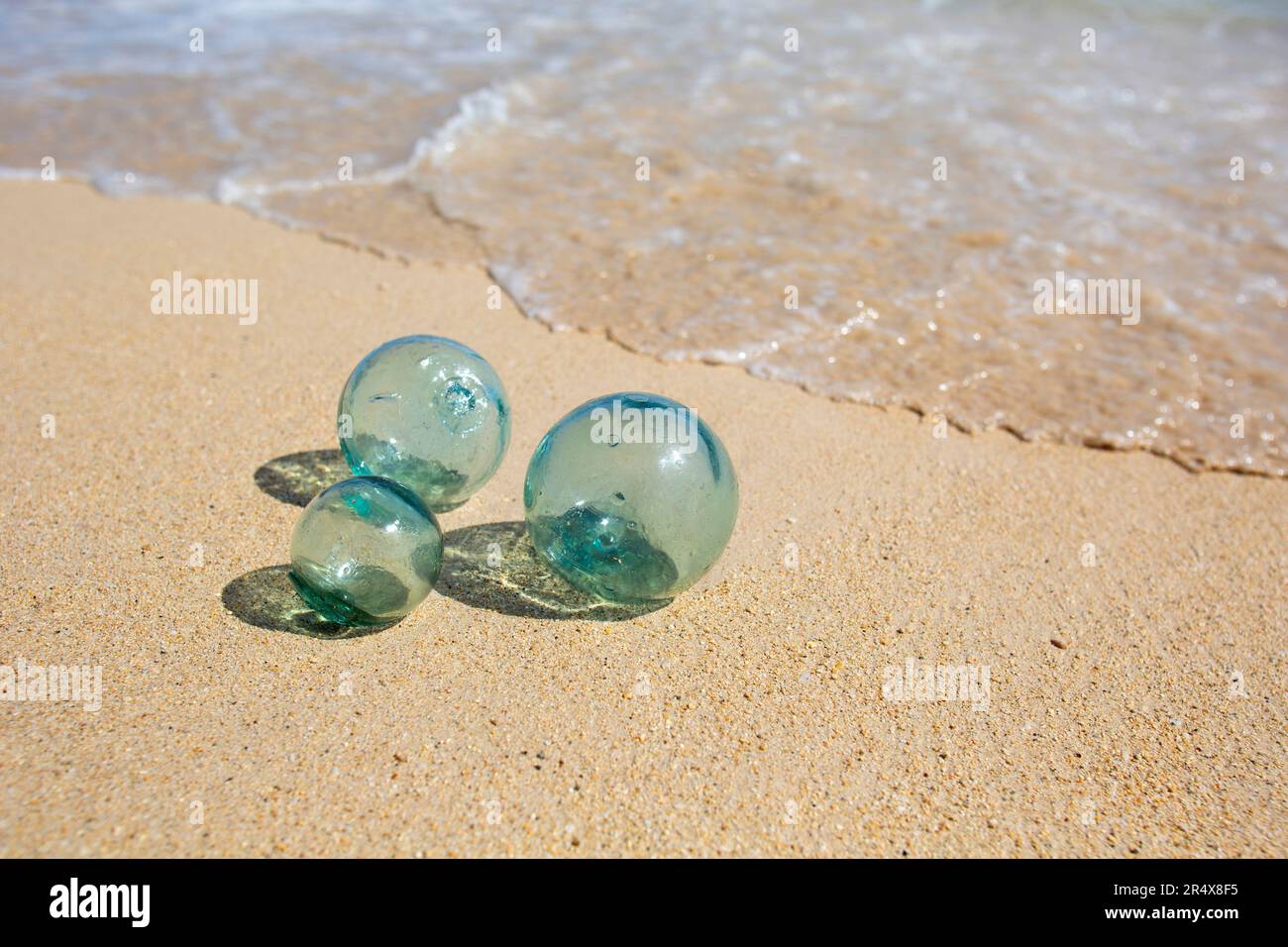 Three, glass Japanese fishing balls (floats) on the wet sand of the ...