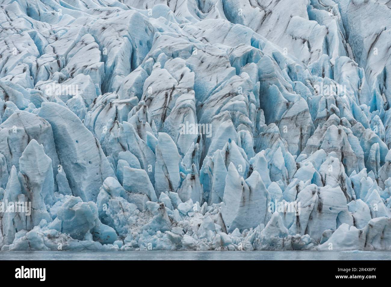 Stunning view of the silt streaked, jagged blue ice shapes of a glacier ...