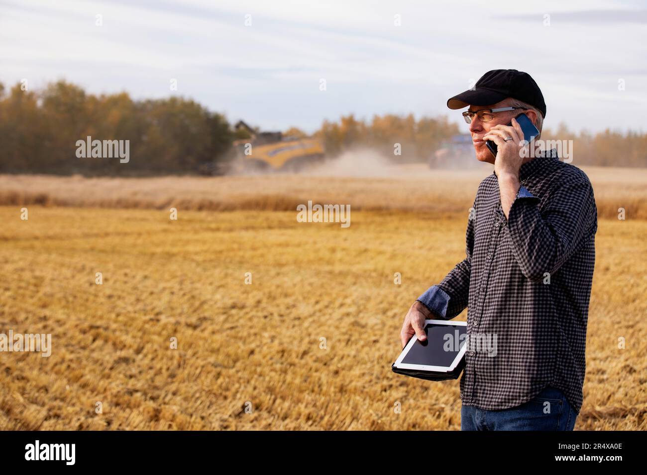 Farmer using a tablet to manage his harvest and talking on his ...