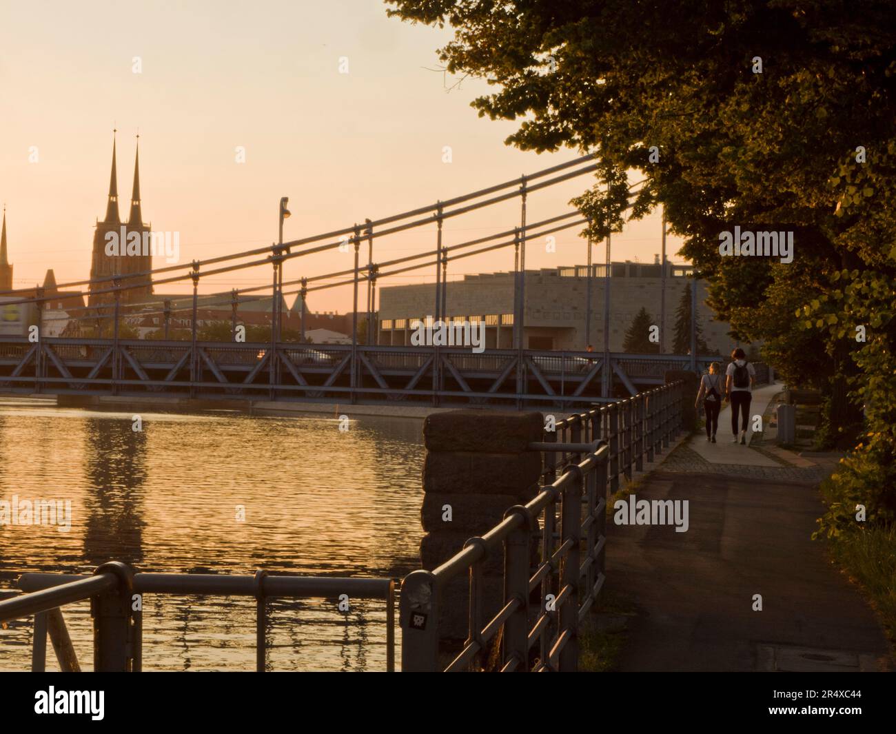 Couple walking along river Odra promenade at sunset with iron bridge ...