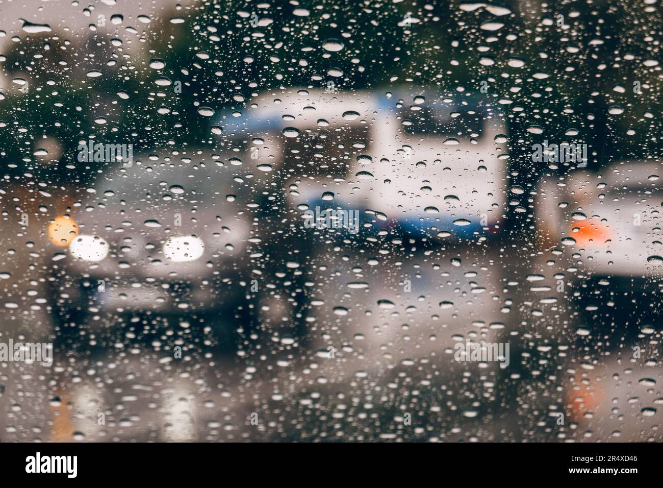 Rainy city background. Moving cars and bus seen from raindrop-covered window of passing car ...