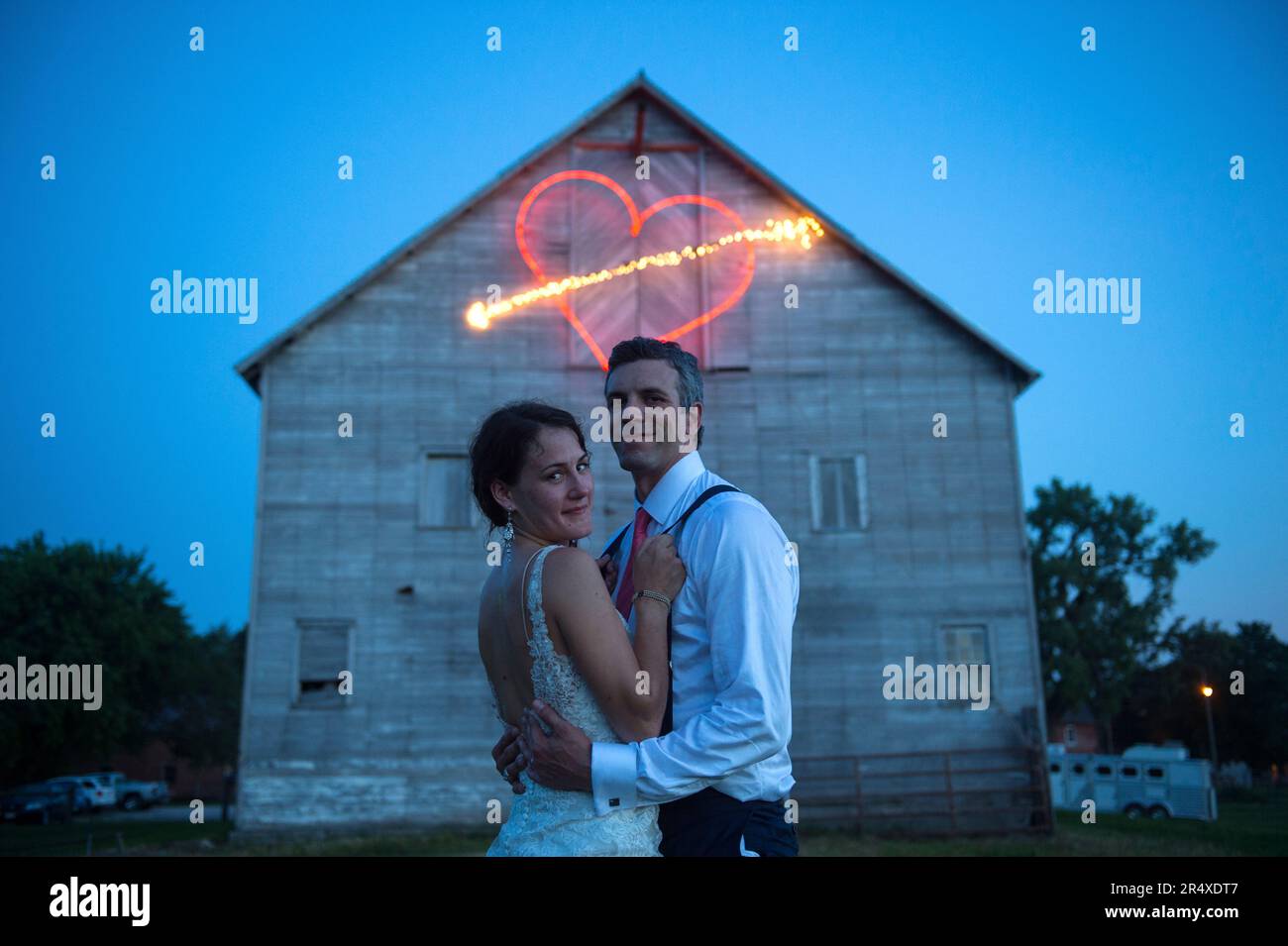 Embracing newlywed couple in front of barn with heart shape made from ...
