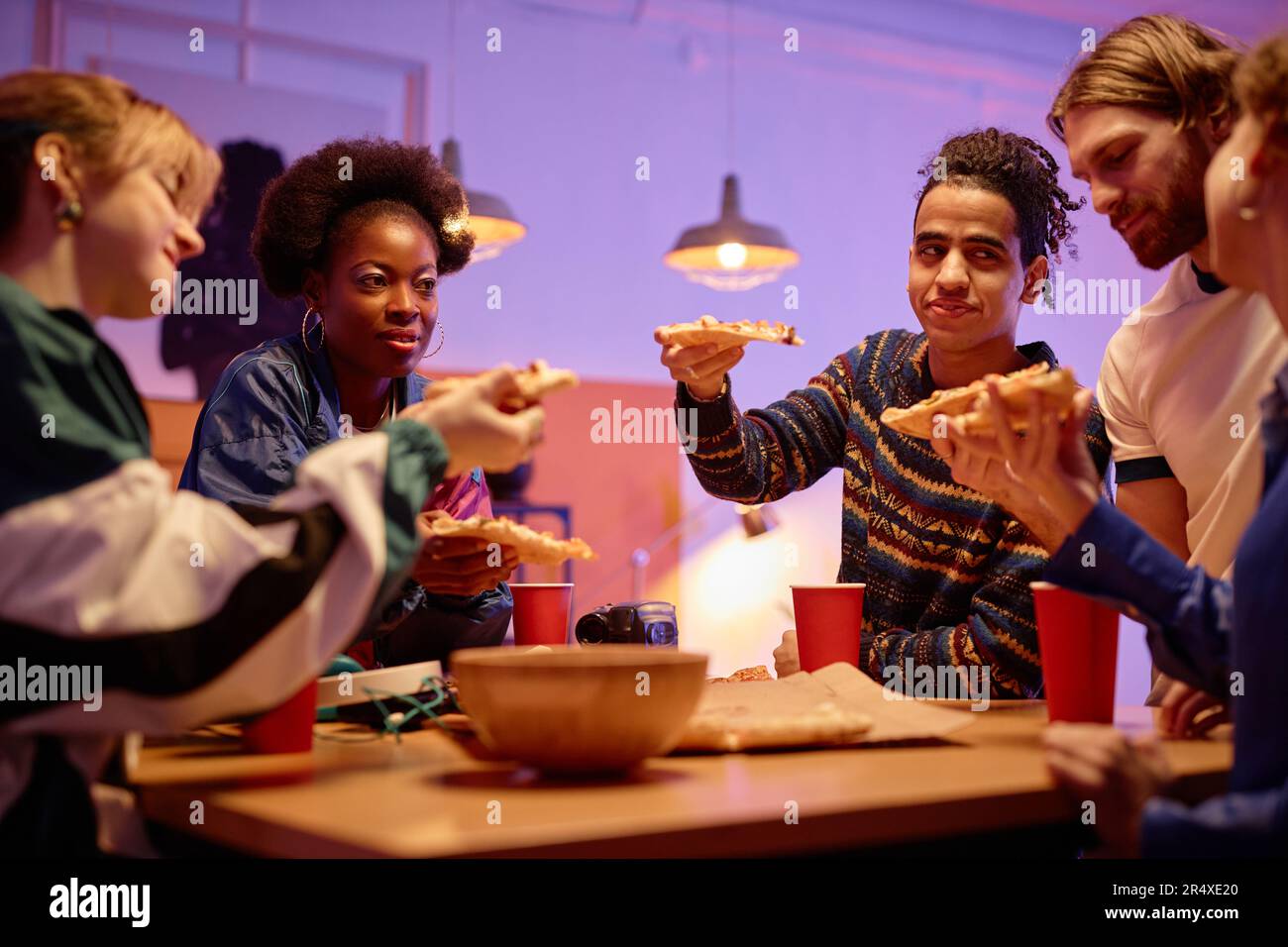 Diverse group of young people eating pizza at house party 80s style ...