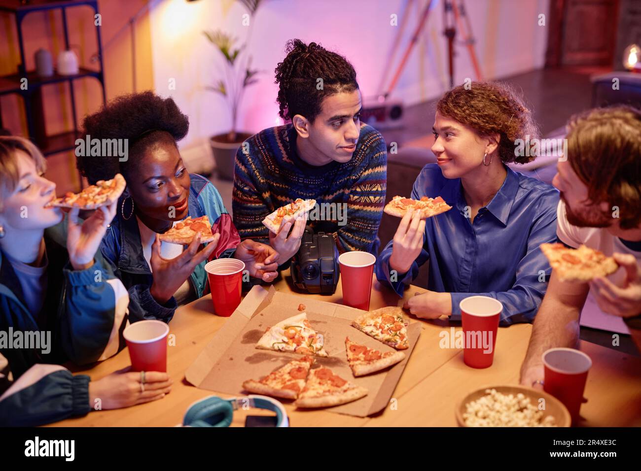 High angle view at group of young people eating pizza at house party ...