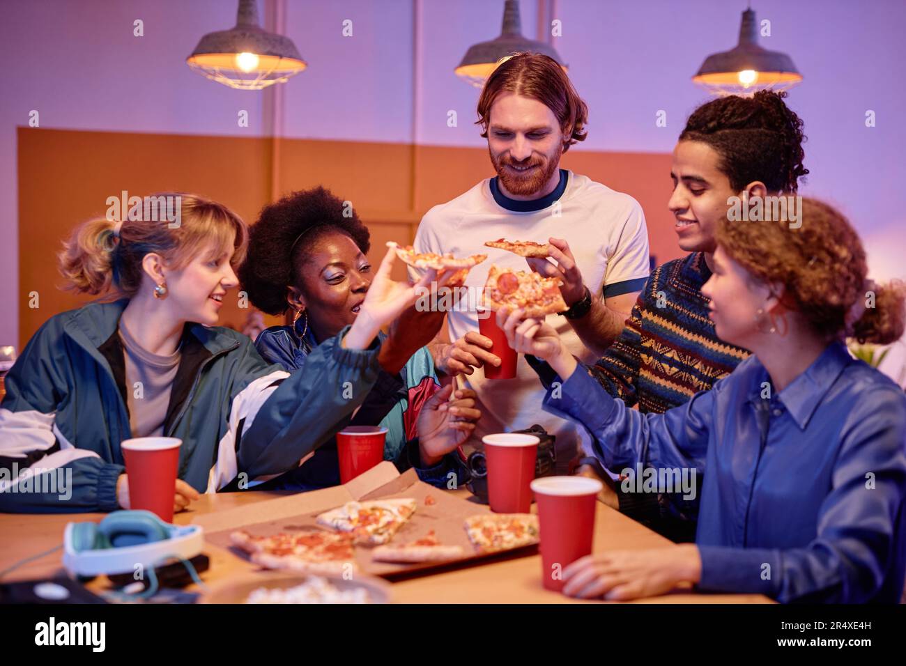 Diverse group of young people eating pizza at house party 80s style ...