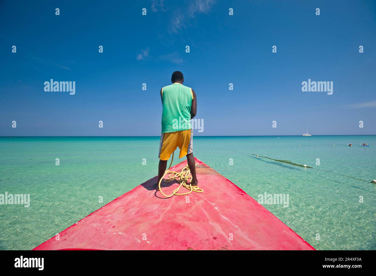 Man pulls up the anchor from the bow of a boat in the Caribbean; Negril ...