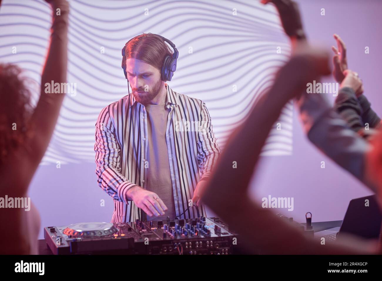 Portrait of long haired DJ by turntable in neon lights entertaining ...