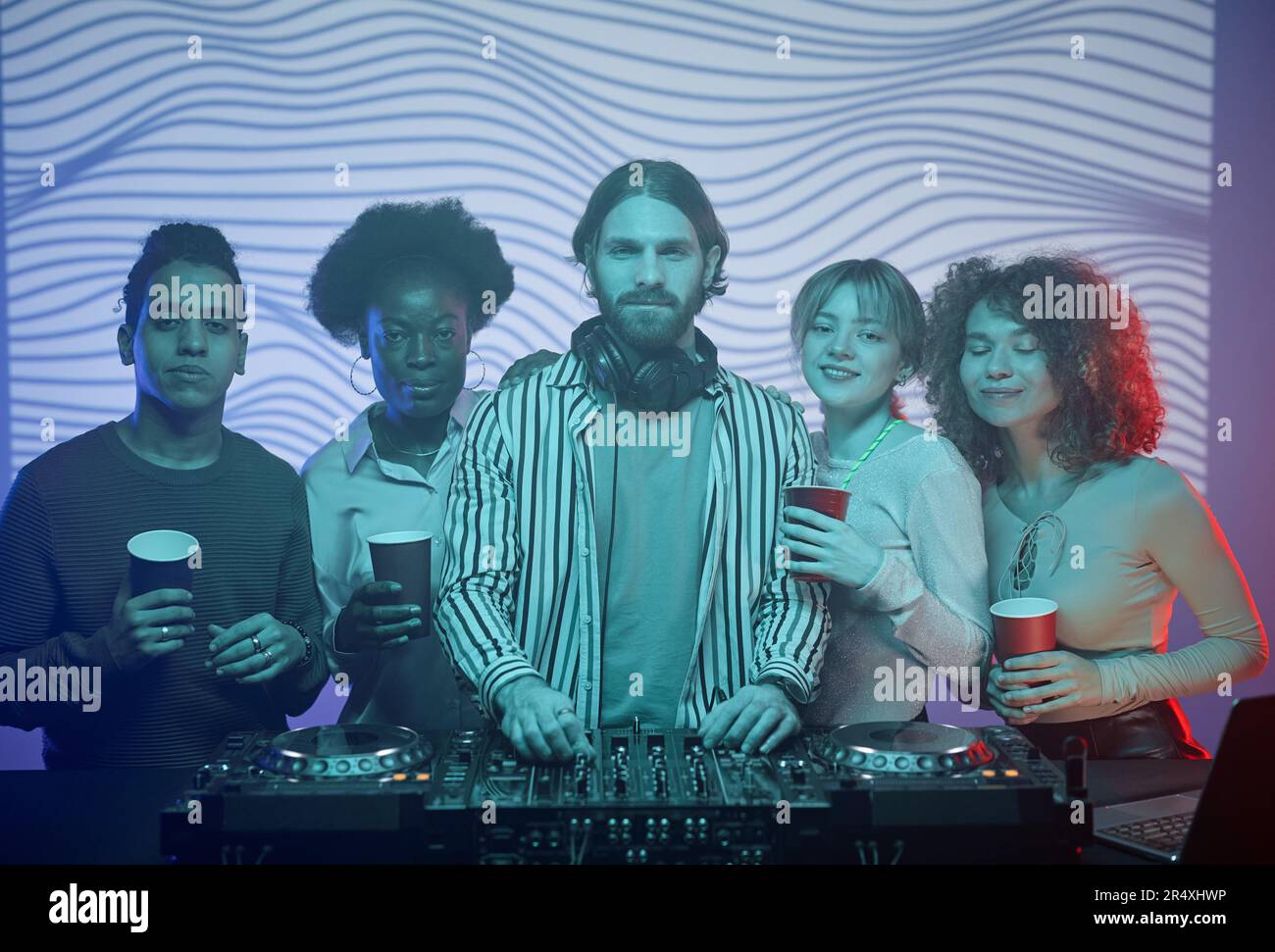 Waist up portrait of long haired DJ with diverse group of people taking ...
