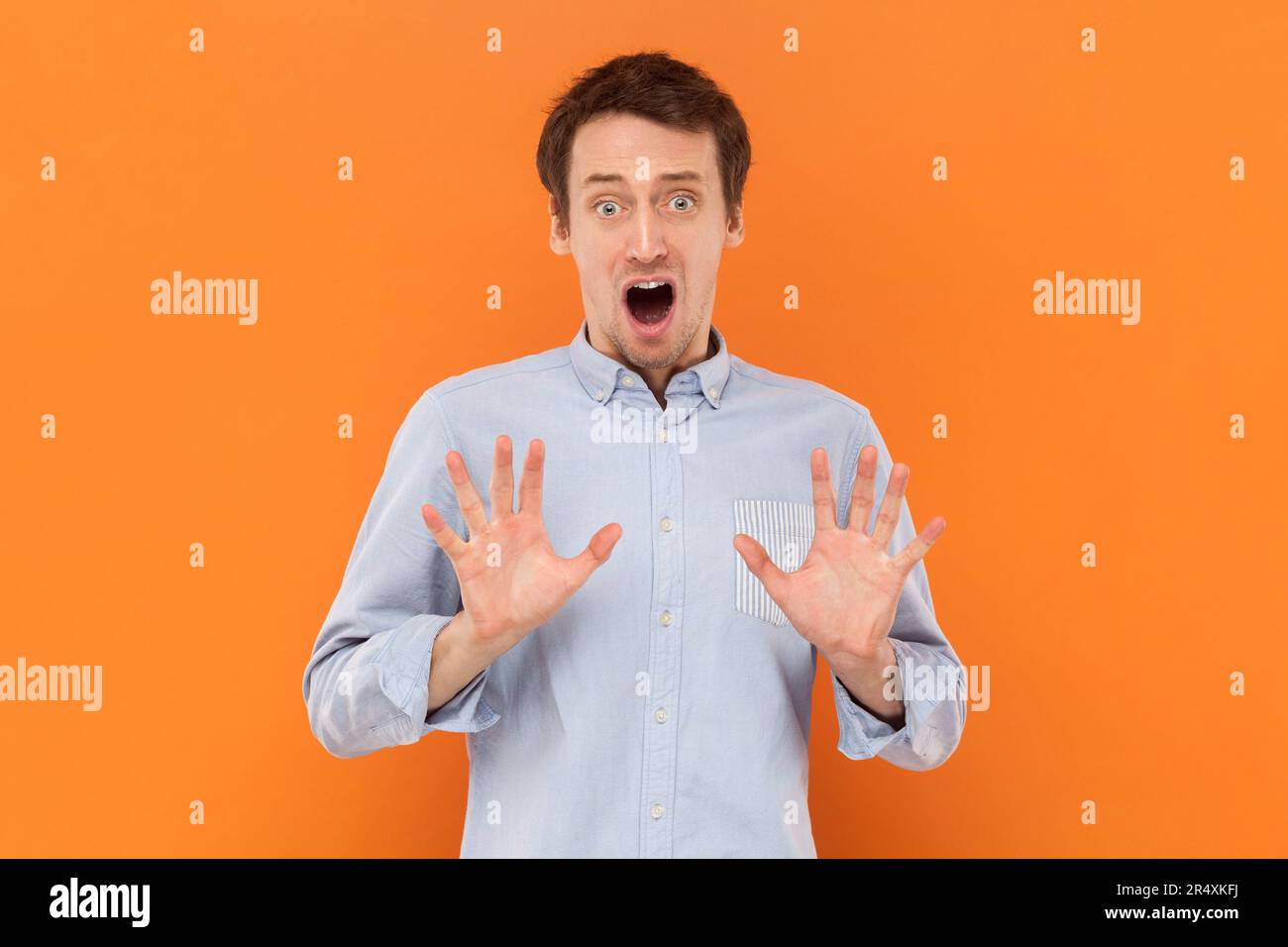 Portrait of scared frighten young adult man standing with raised arms ...