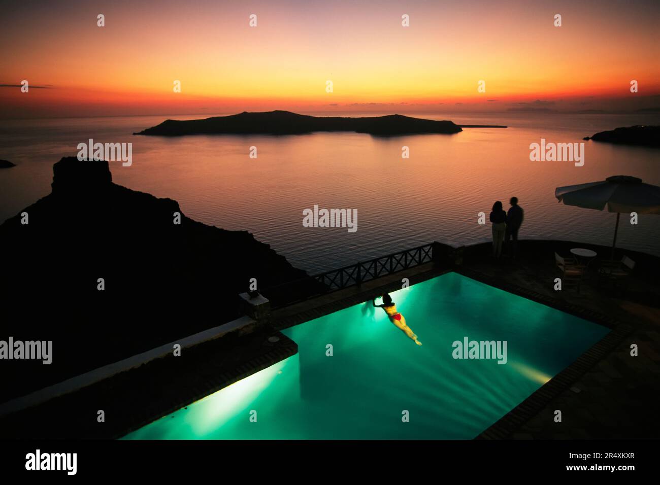 Couple and a woman in a pool watching a scenic sunset; Santorini ...