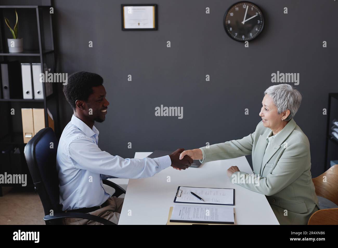 Side view portrait of smiling senior woman shaking hands with employer ...