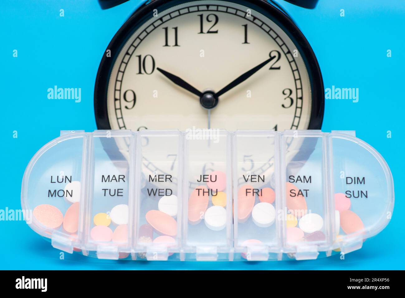 Black alarm clock and 7 day plastic pill organizer on blue background ...