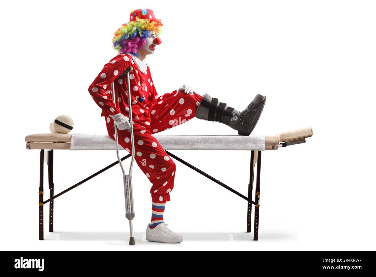 Injured clown with a walking brace sitting on a therapy bed isolated on ...
