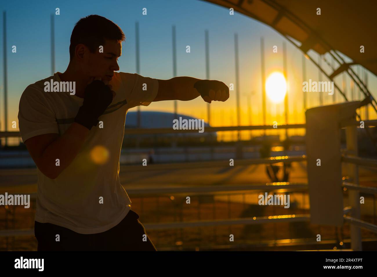 A man trains in boxing at the stadium at sunset. Athlete silhouette ...