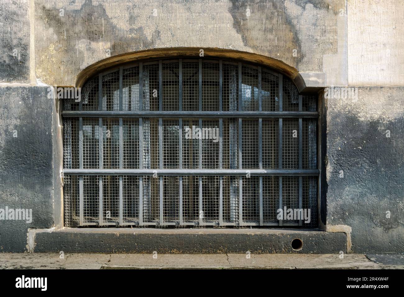 Arched basement window with iron bars on the background of an old stone ...