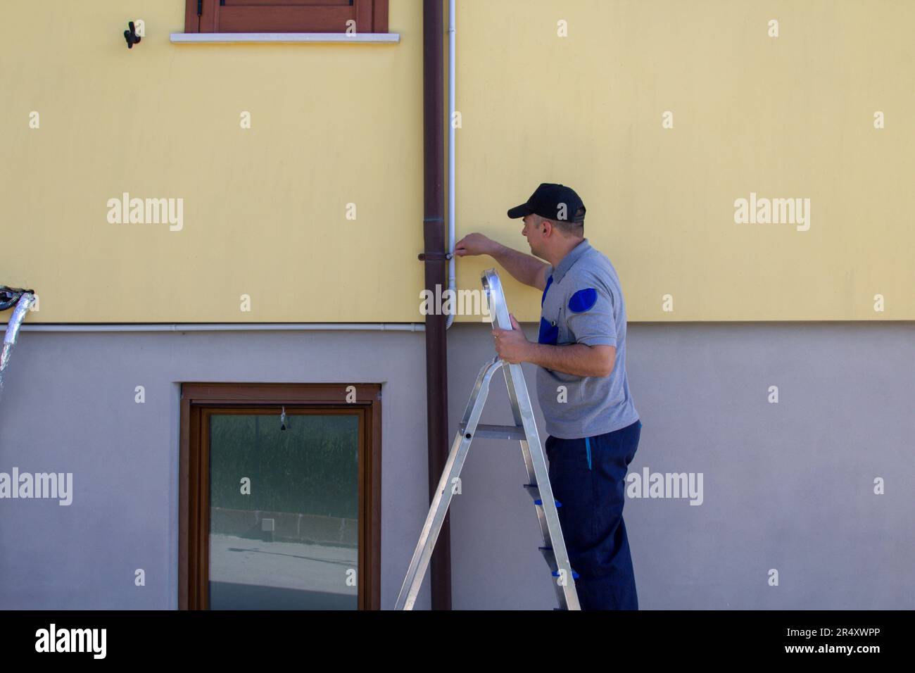 Image of a handyman on a stepladder assembling a gutter channel. Do-it ...