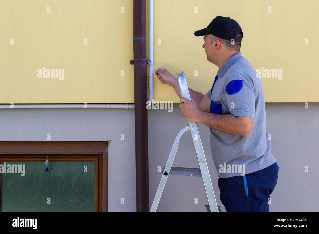 Image of a handyman on a stepladder assembling a gutter channel. Do-it ...
