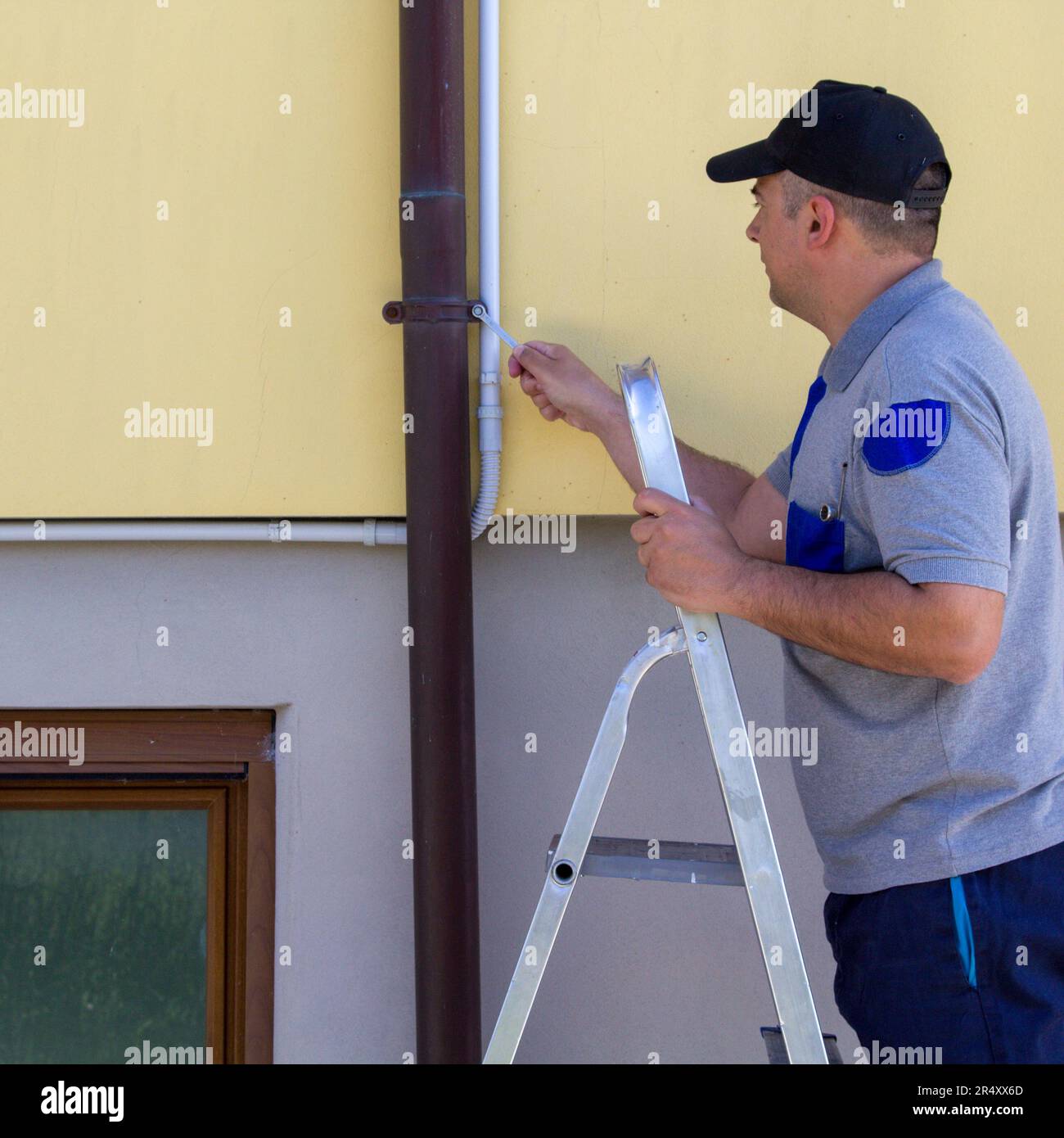 Image of a handyman on a stepladder assembling a gutter channel. Do-it ...