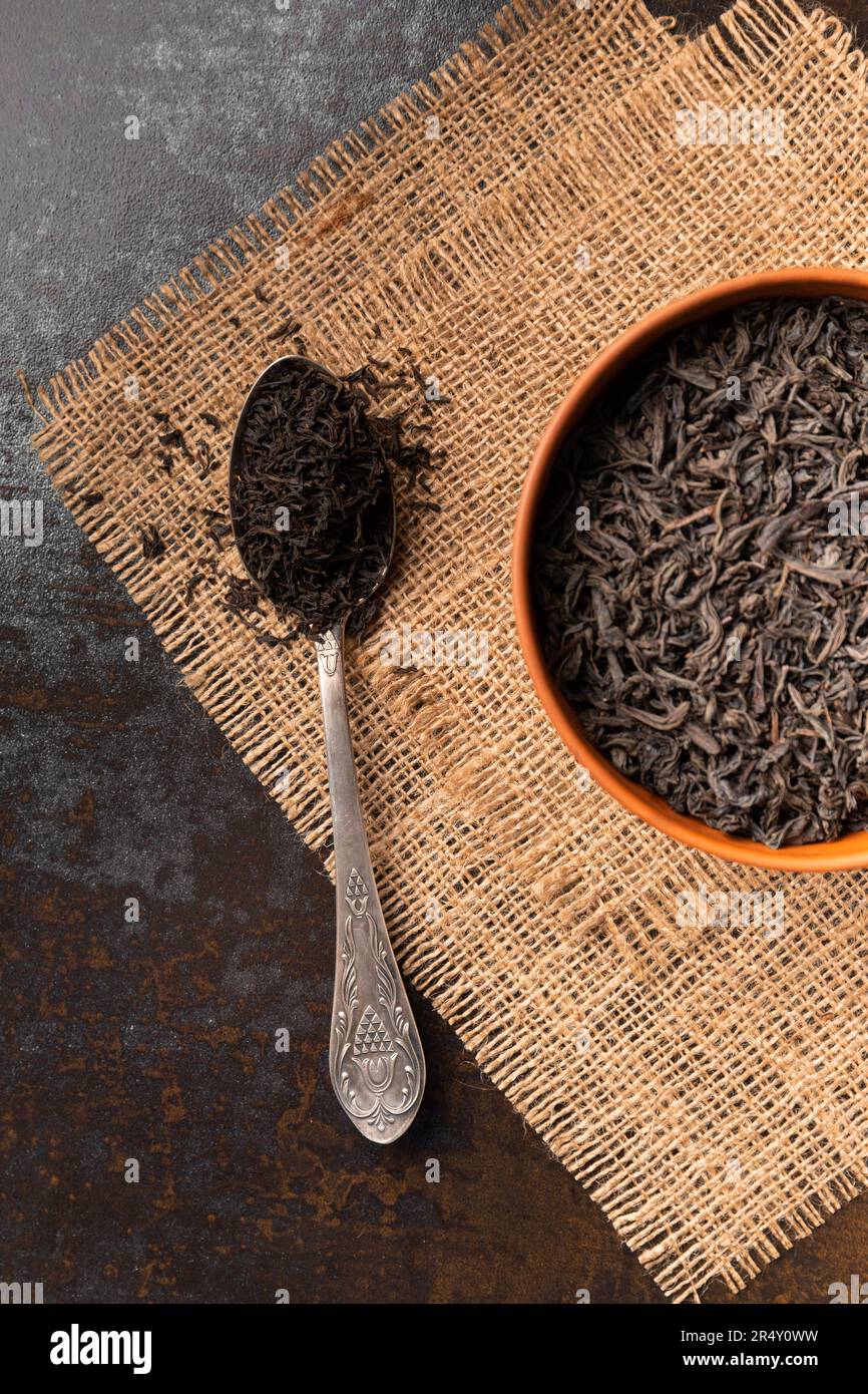 Dry black tea leaves in a clay bowl and a vintage spoon on a dark ...