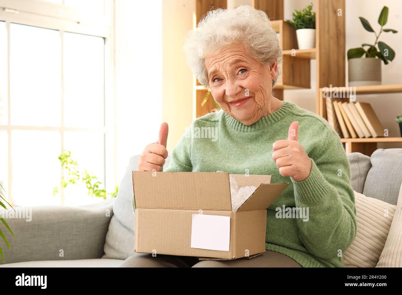 Senior woman with open parcel showing thumbs-up at home Stock Photo - Alamy