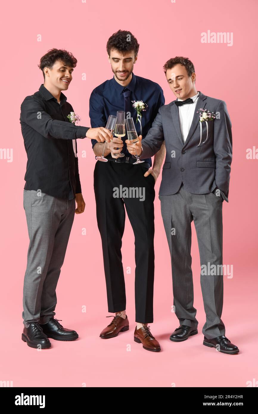 Young men dressed for prom with glasses of champagne on pink background ...